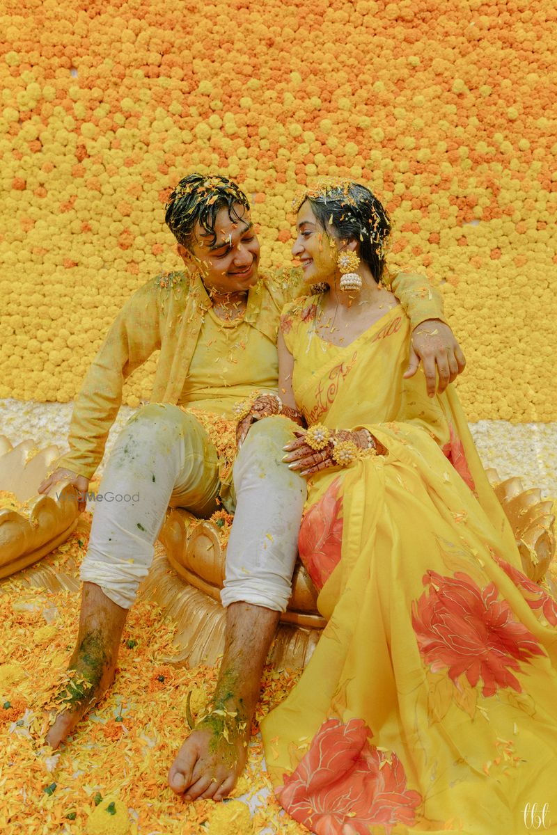 Photo of happy haldi couple shot against floral wall backdrop